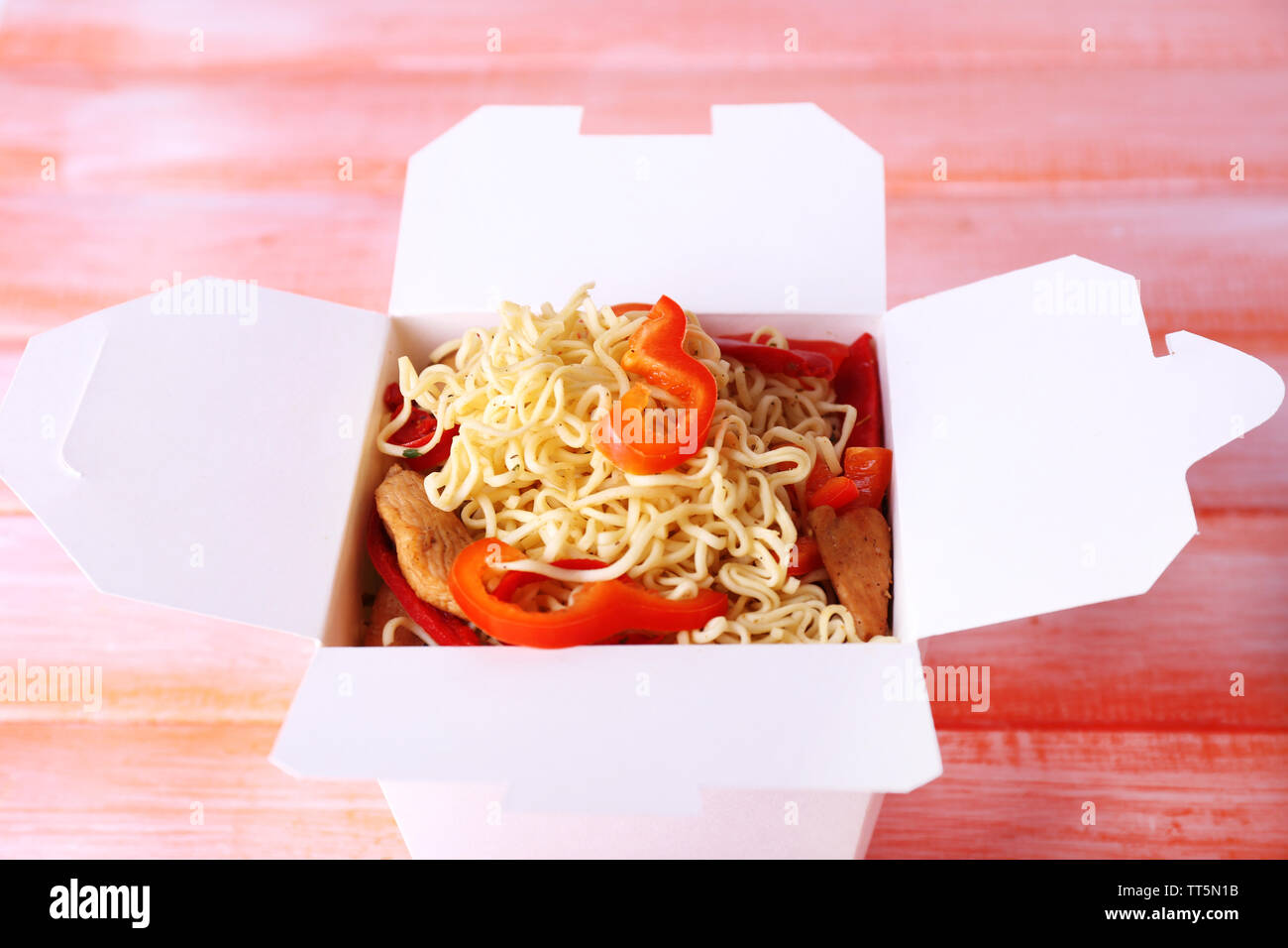 Chinese noodles with meat and pepper in takeaway box on pink background ...
