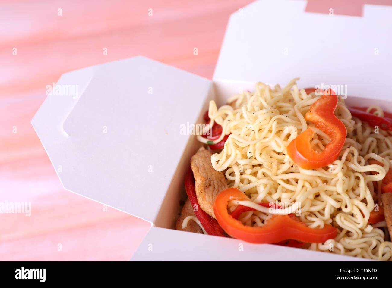Chinese noodles with meat and pepper in takeaway box on pink background ...