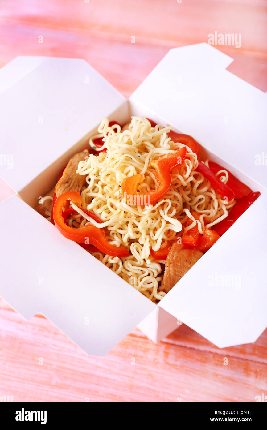 Chinese noodles with meat and pepper in takeaway box on pink background ...