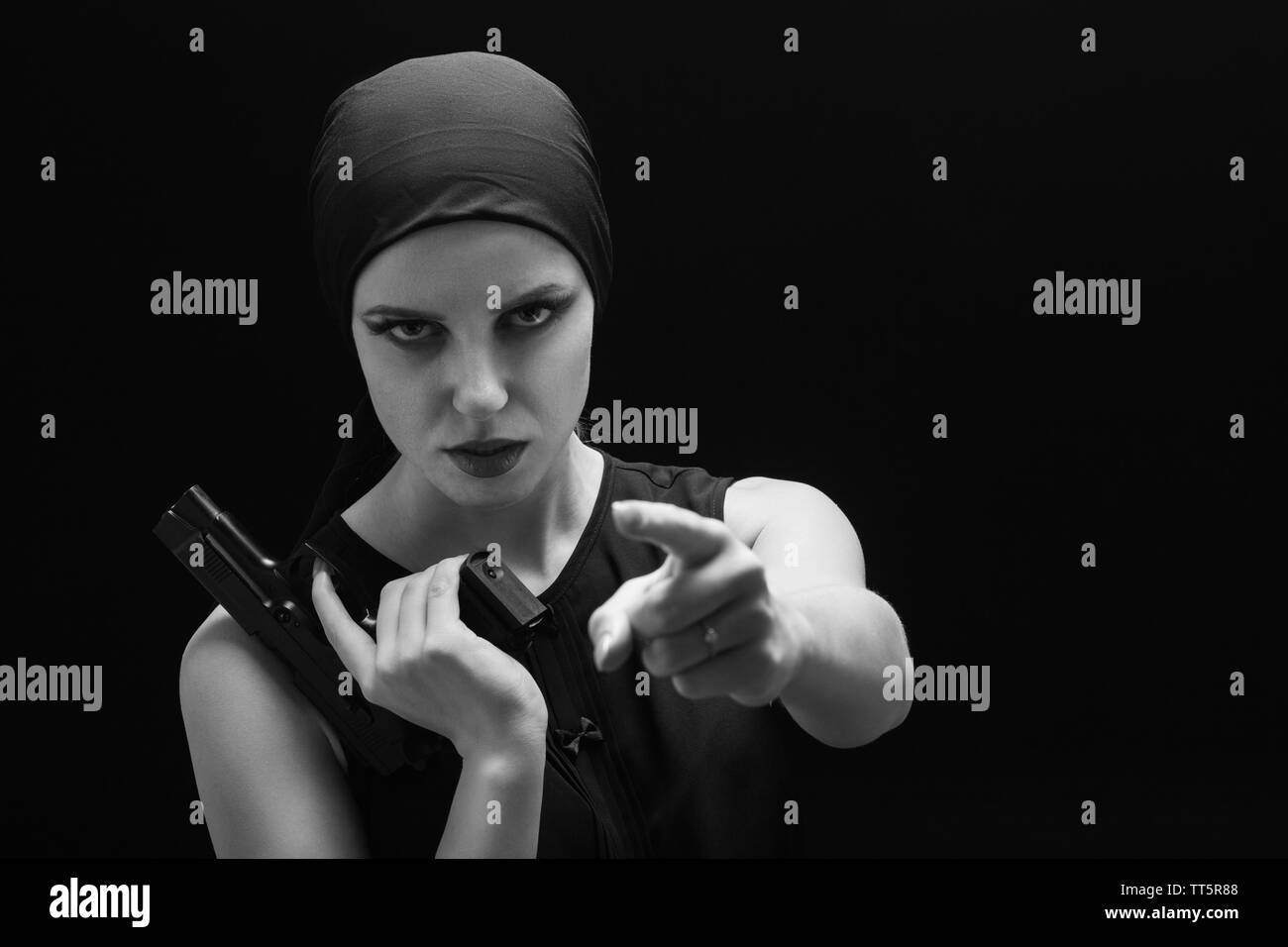 serious girl with gun point at camera on black background, monochrome ...