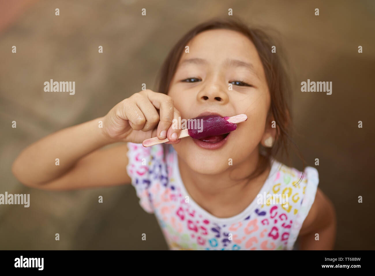 Small girl bites ice cream on wooden stick above top view Stock Photo ...