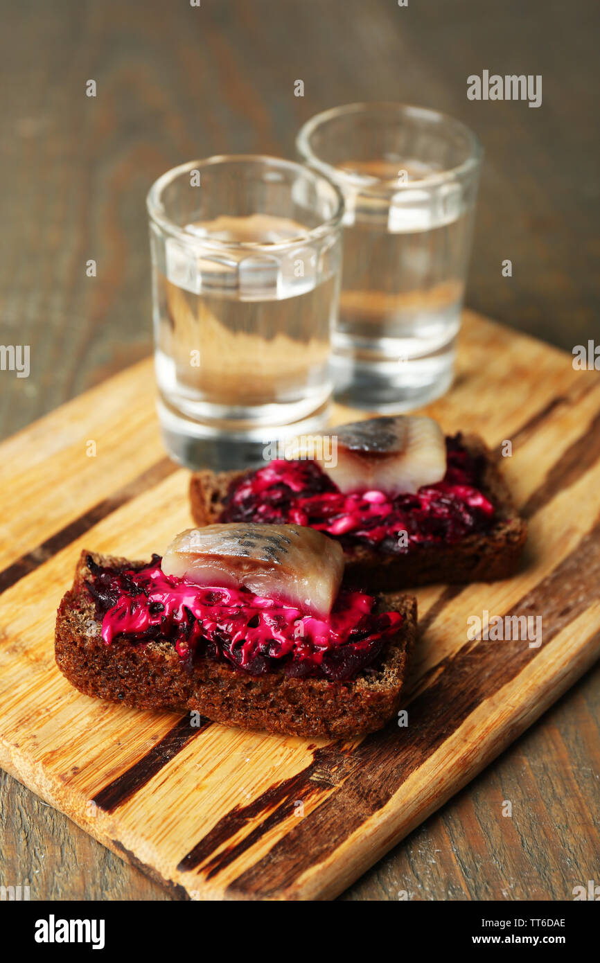 Canape herring with beets on rye toasts, on wooden board, and glass of ...