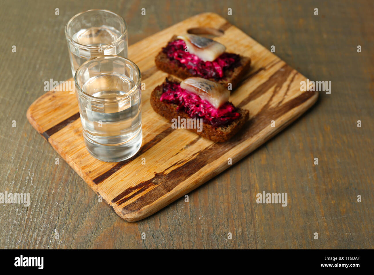 Canape herring with beets on rye toasts, on wooden board, and glass of ...