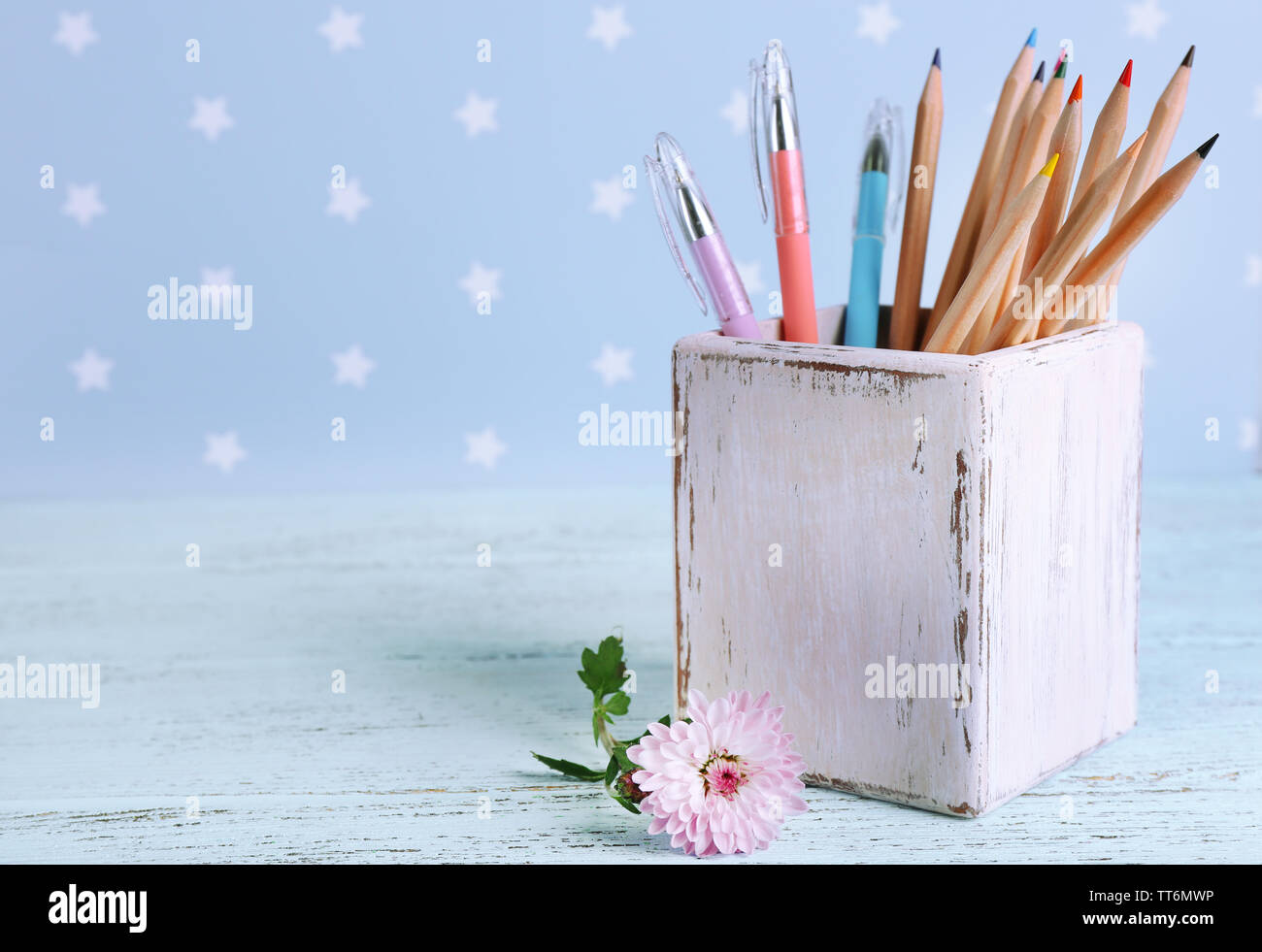 Different pens and pencils near flower on color wooden table on color ...