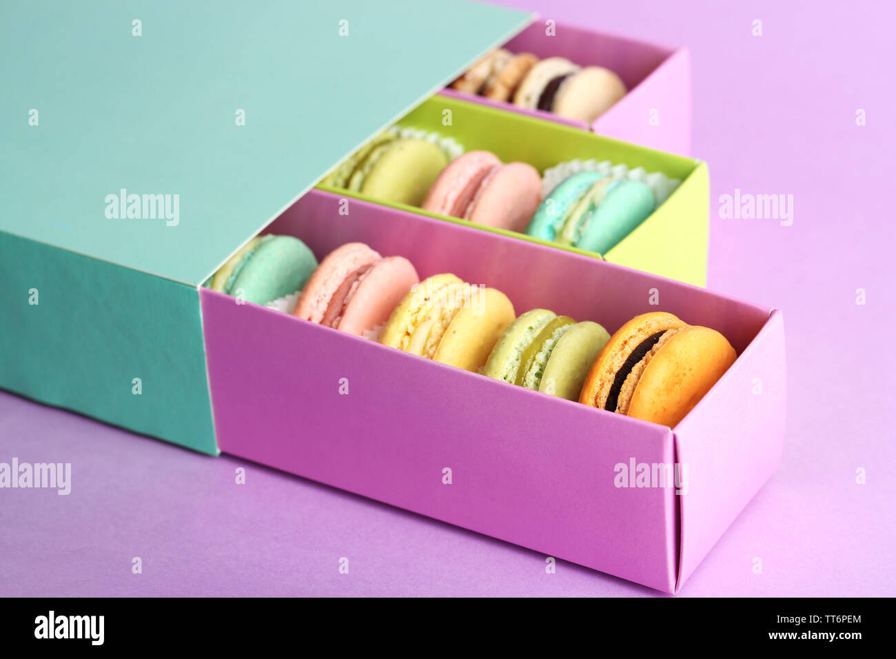Assortment of gentle colorful macaroons in box on color background ...