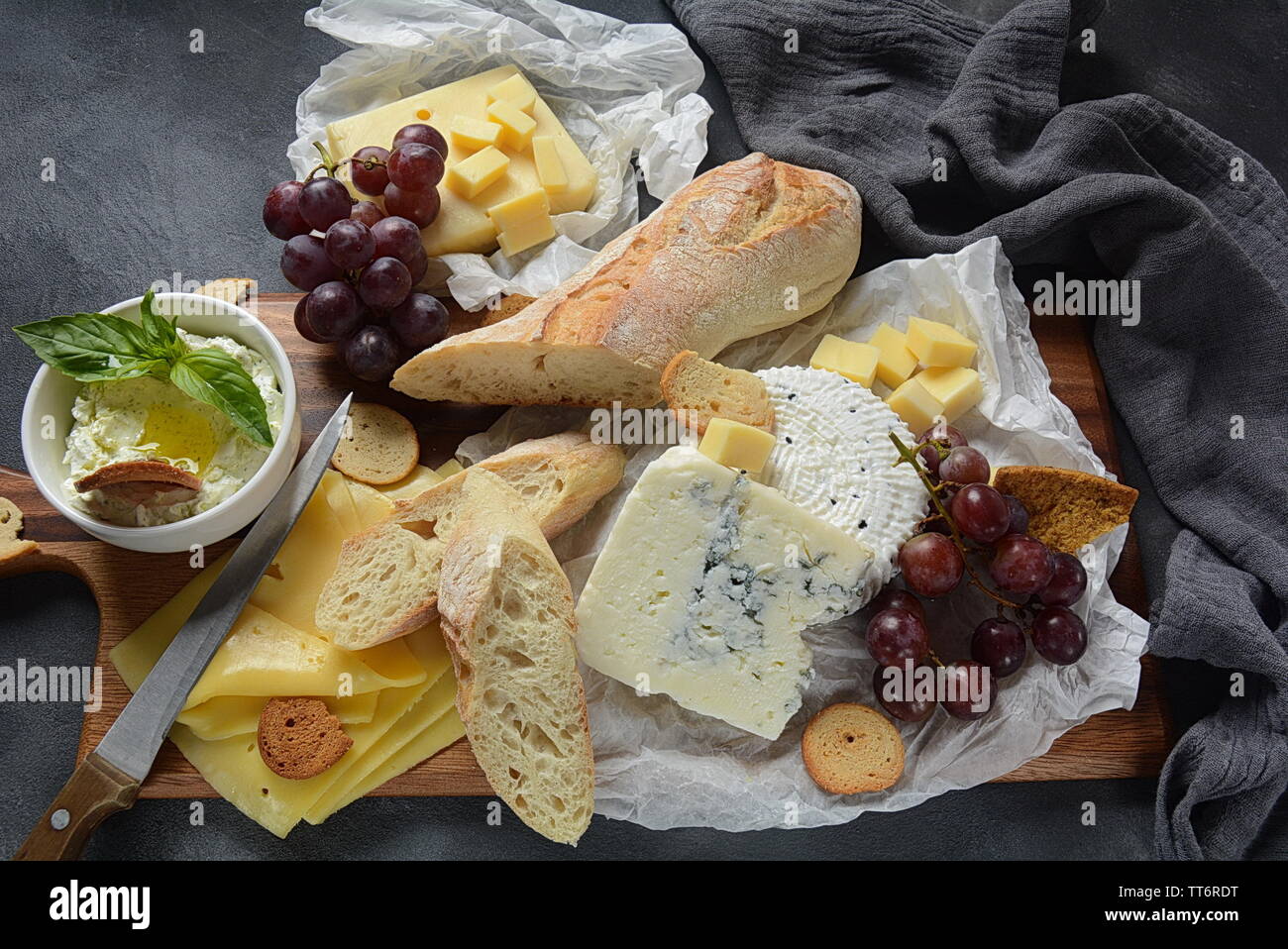 Cheese platter with assorted cheese, grapes, snacks on dark background ...