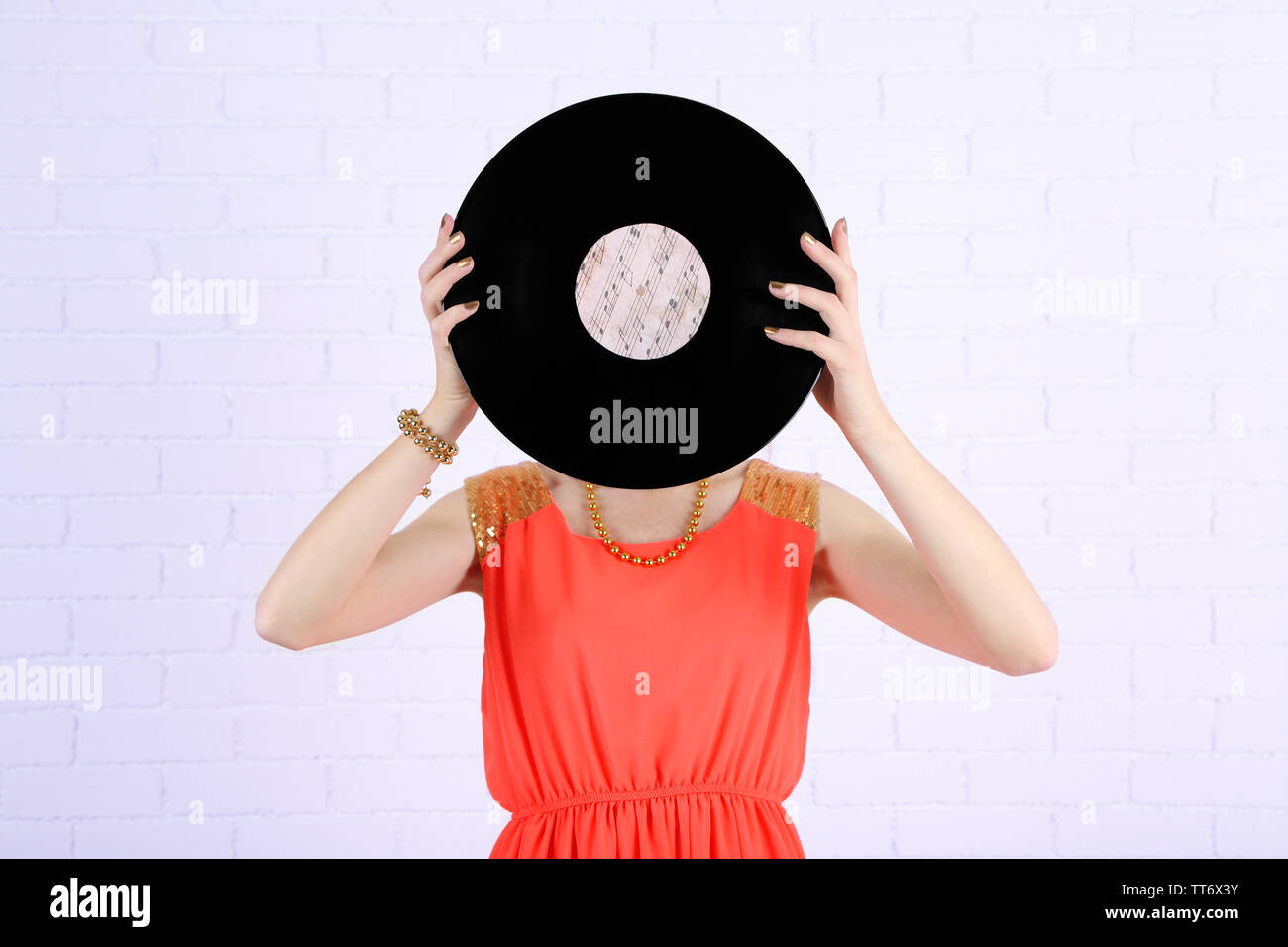 Young woman holding retro record in front of face, on shiny background ...