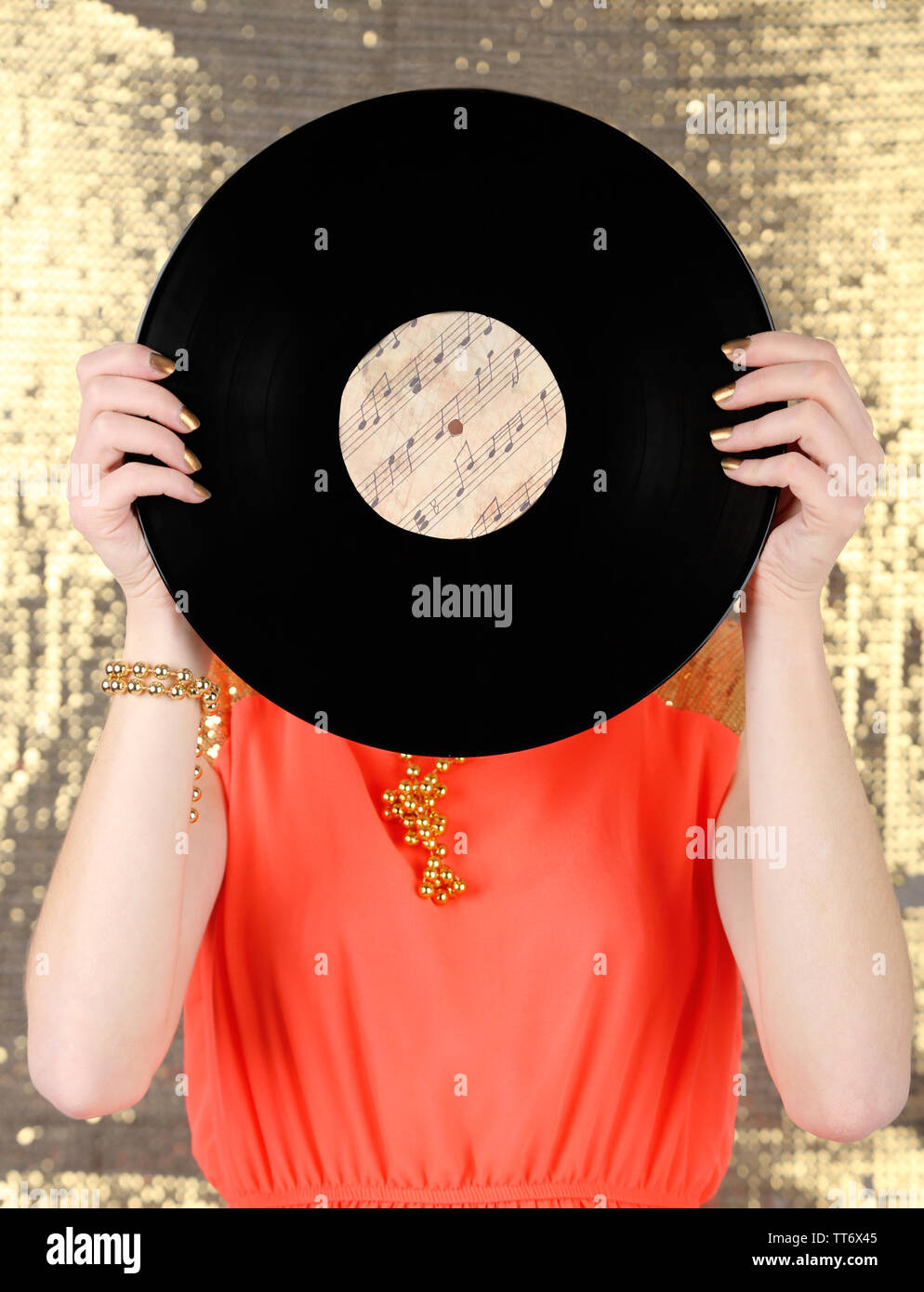 Young woman holding retro record in front of face, on shiny background ...