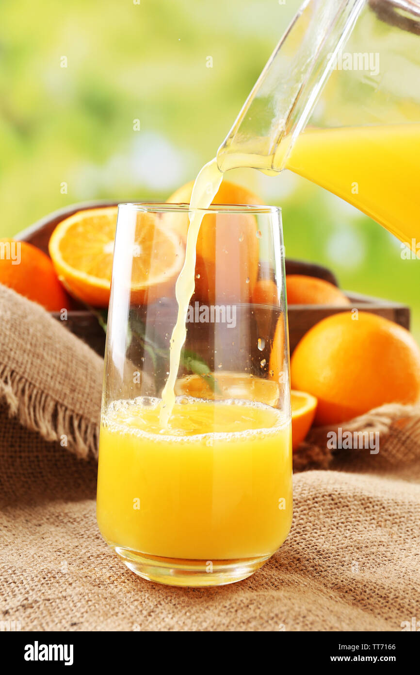 Pouring orange juice from glass carafe, on wooden table and bright ...