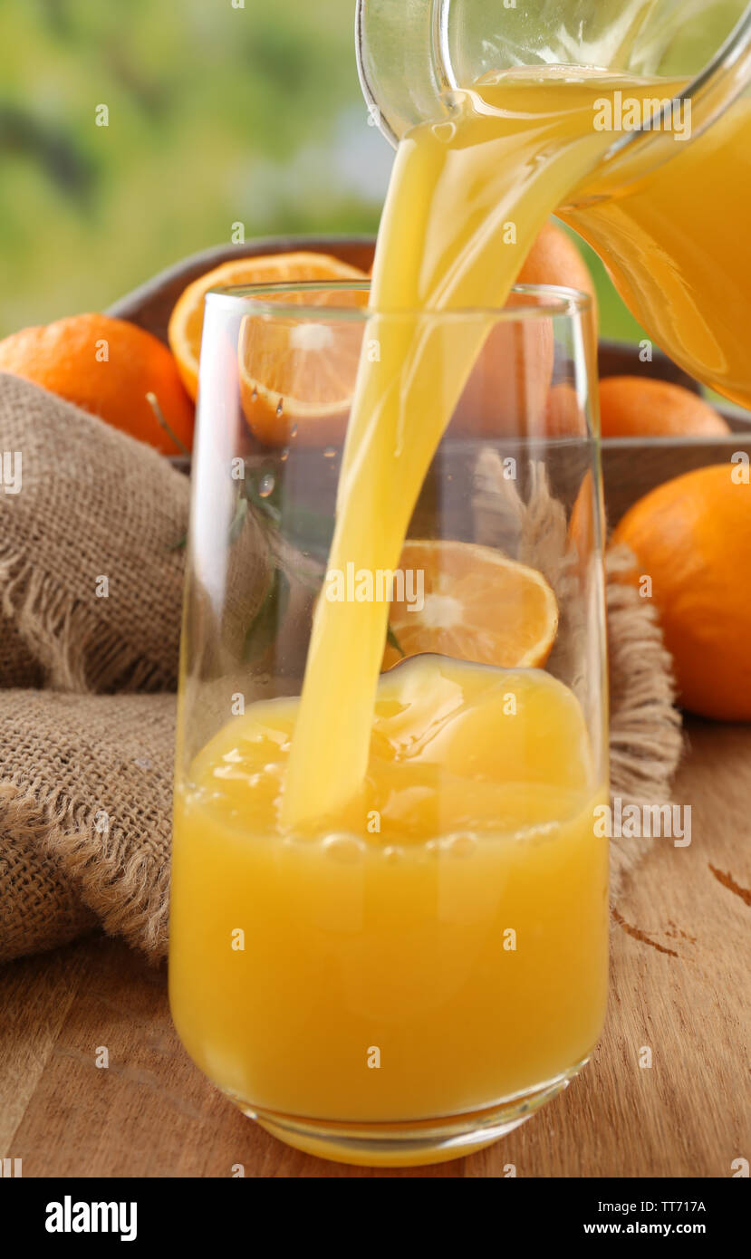 Pouring orange juice from glass carafe, on wooden table and bright ...