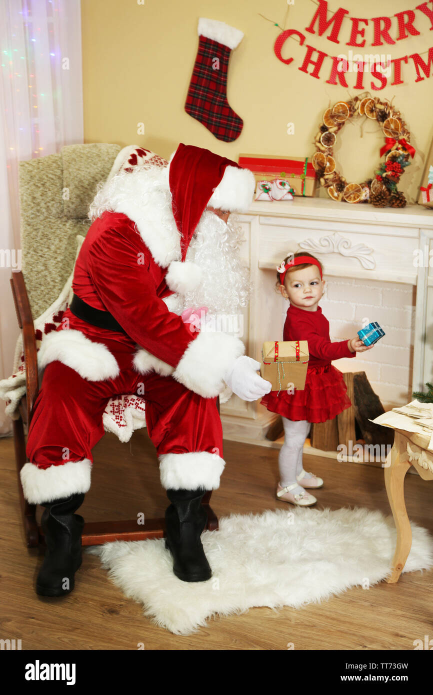 Santa Claus giving present to little cute girl near fireplace and ...