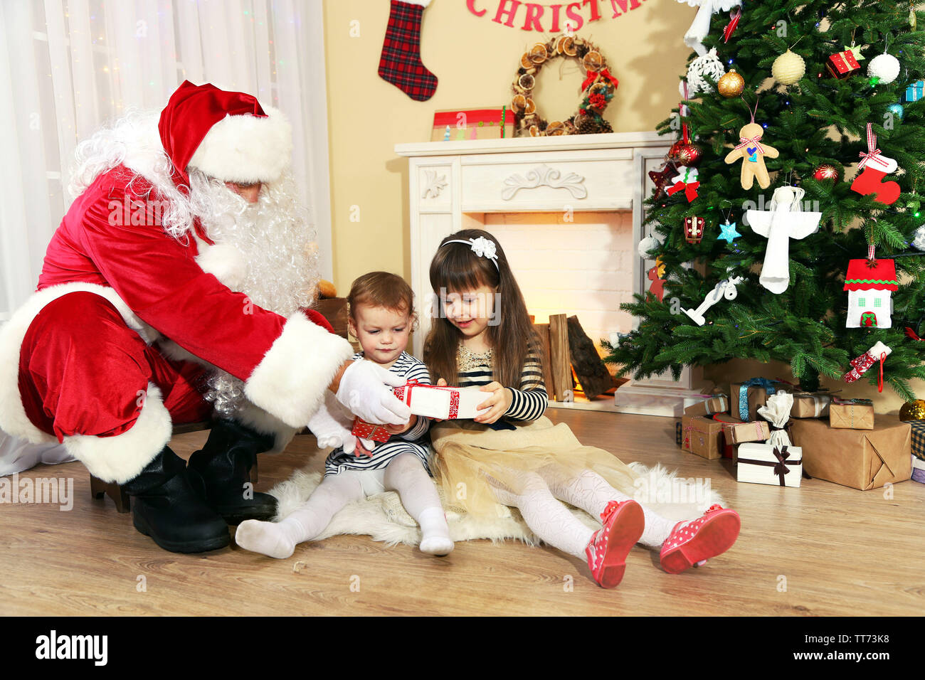 Santa Claus giving present to little cute girls near fireplace and ...