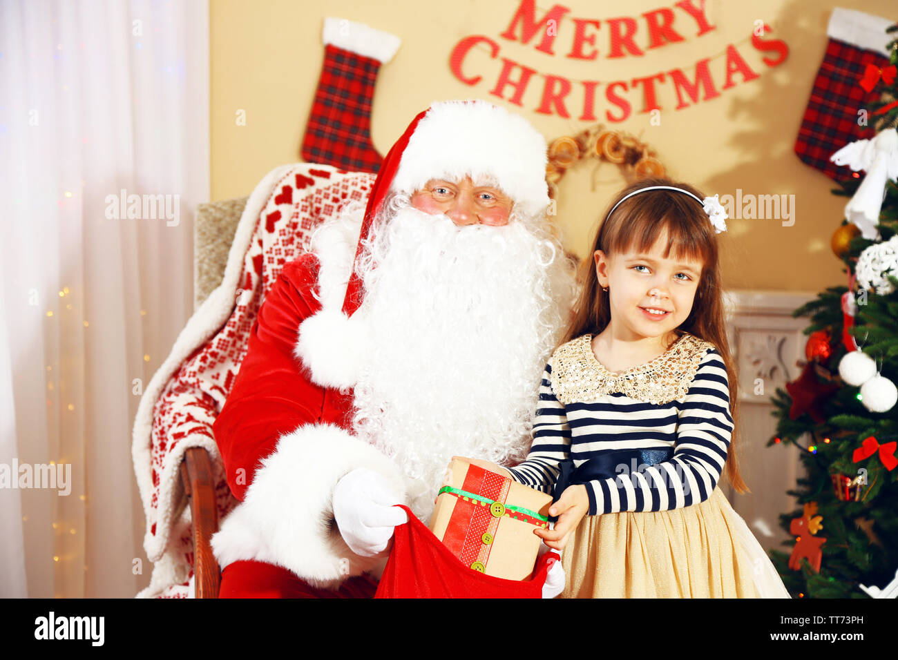 Santa Claus giving present to little cute girl near Christmas tree at ...