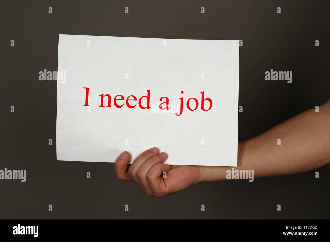 Sheet of paper with inscription I need a job in male hand on dark ...