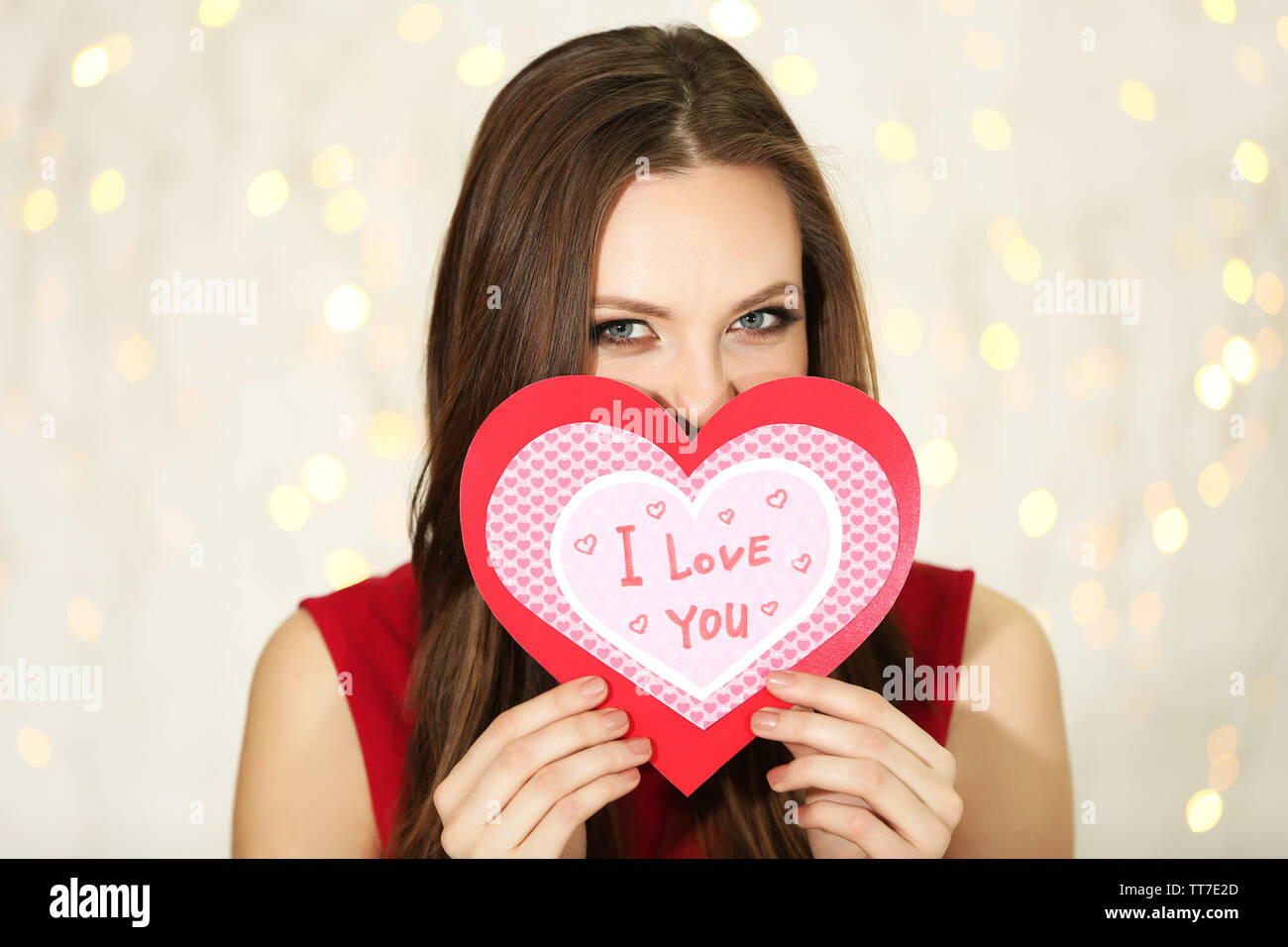 Smiling girl holding Valentines card with greetings on lights ...