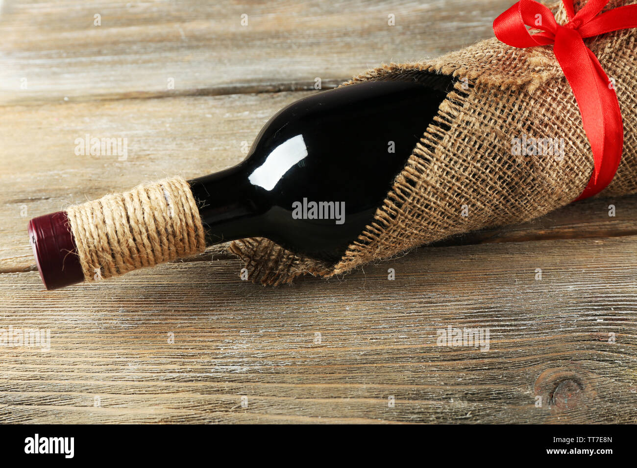 Red wine bottle wrapped in burlap cloth on wooden planks background ...