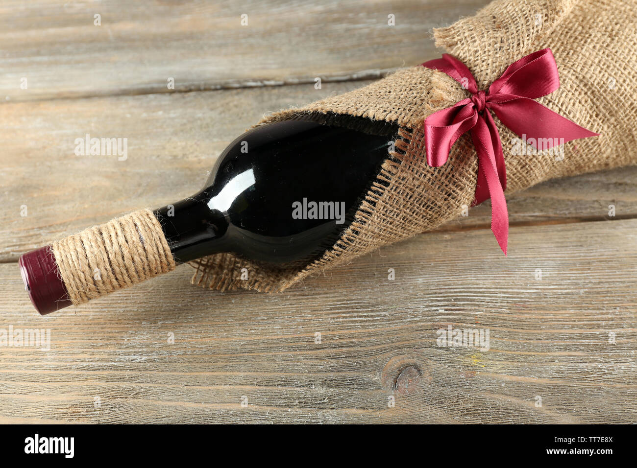 Red wine bottle wrapped in burlap cloth on wooden planks background ...