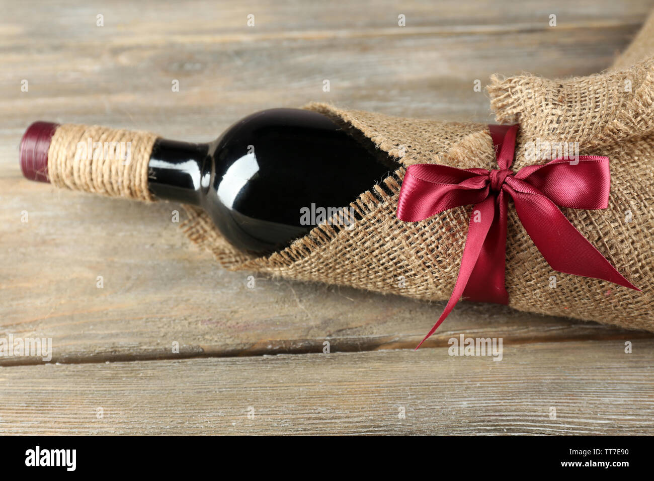 Red wine bottle wrapped in burlap cloth on wooden planks background ...
