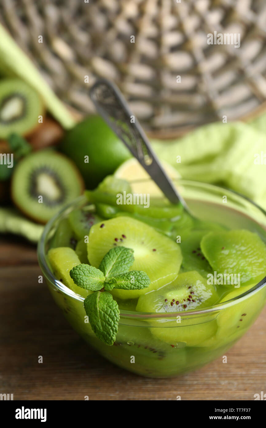 Tasty kiwi jam in glass bowl on wooden table, on wicker mat background ...