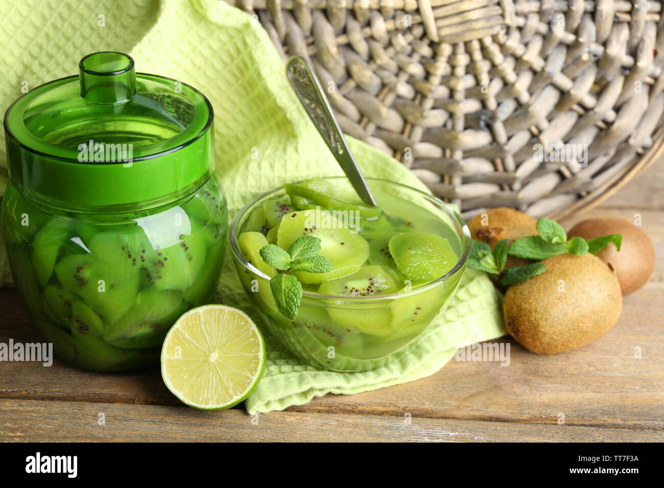 Tasty kiwi jam in glass bowl and jar on wooden table, on wicker mat ...