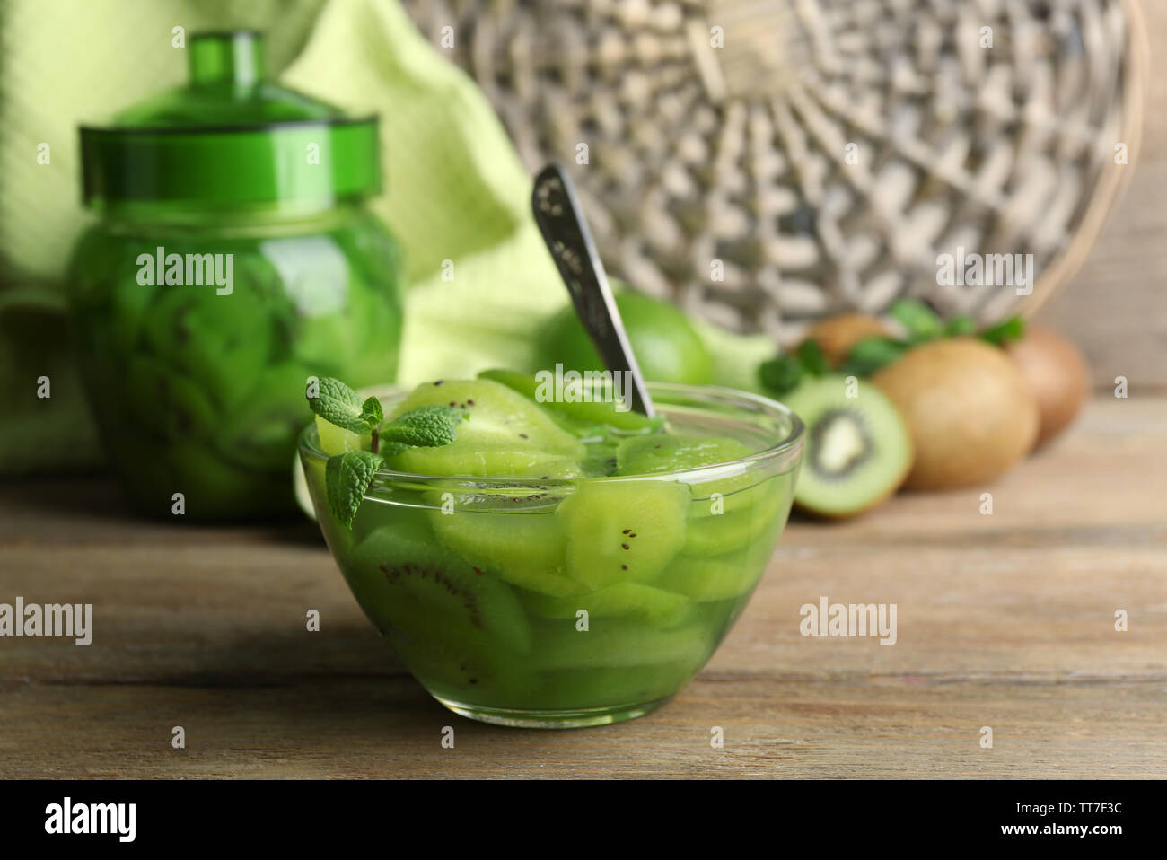 Tasty kiwi jam in glass bowl and jar on wooden table, on wicker mat ...