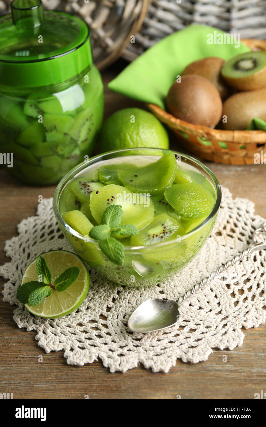 Tasty kiwi jam in glass bowl and jar on wooden table, on wicker mat ...
