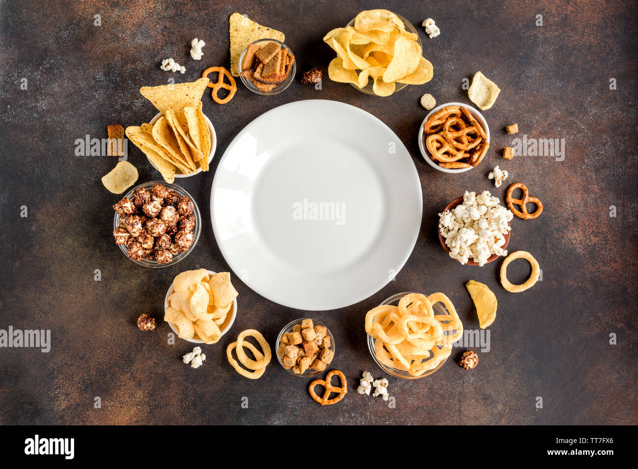 Assortment of Unhealthy Snacks around plate: chips, popcorn, nachos ...