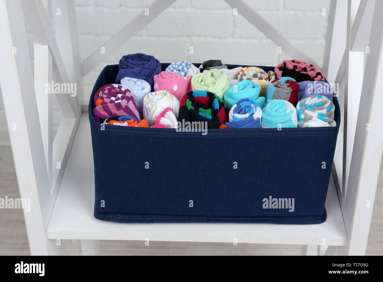 Different socks in textile box on shelf and white brick wall background ...