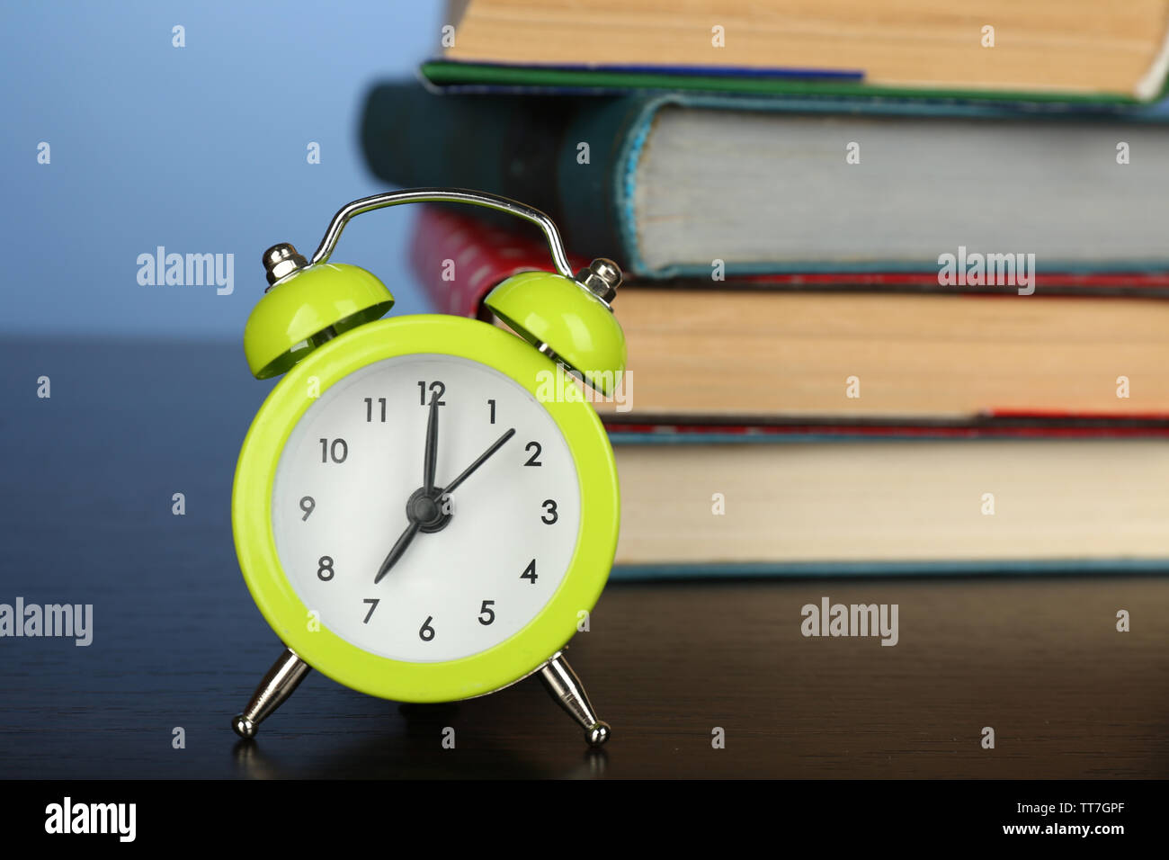 Stack of books with alarm clock on wooden desk and colorful background ...