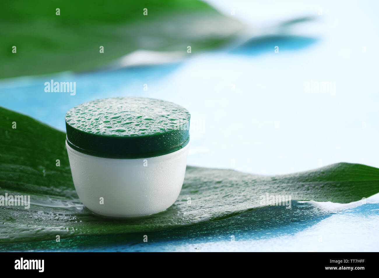Cosmetic cream with water drops on green leaves on light background ...