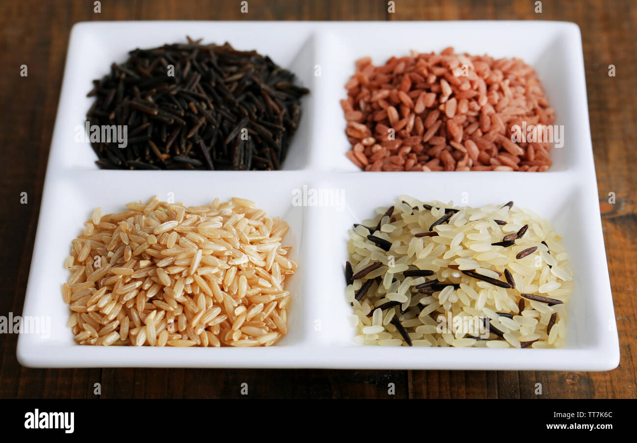 Different types of rice on plate on wooden background Stock Photo - Alamy