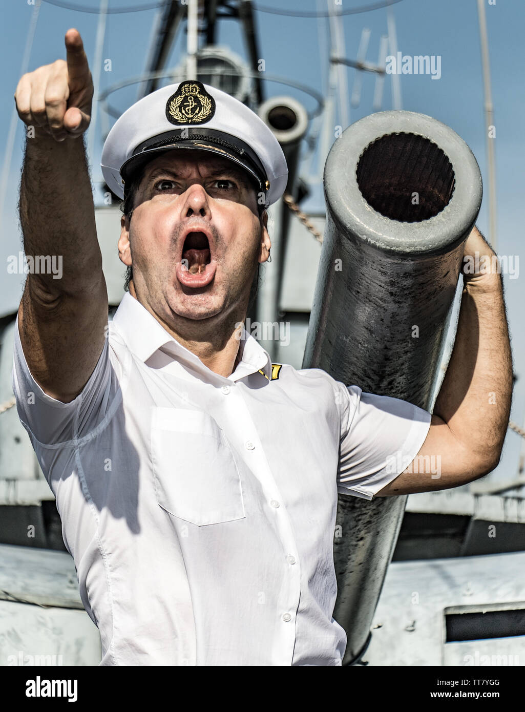 A navy officer standing beside gun and pointing his finger ahead.The ...