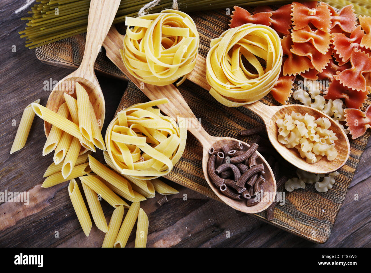 Different types of pasta on cutting board and wooden table background ...