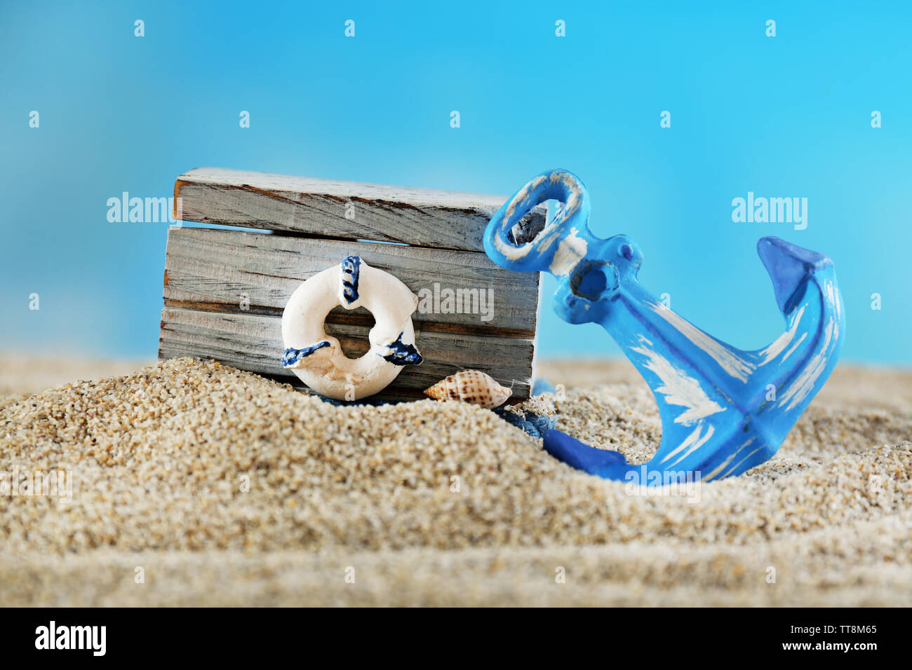 Wooden box with lifebuoy and anchor on sand on blue background Stock ...