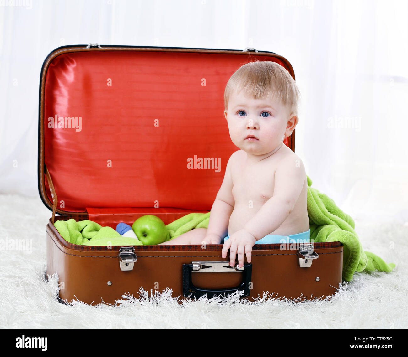 Cute baby boy sitting in big suitcase on carpet, on light background ...