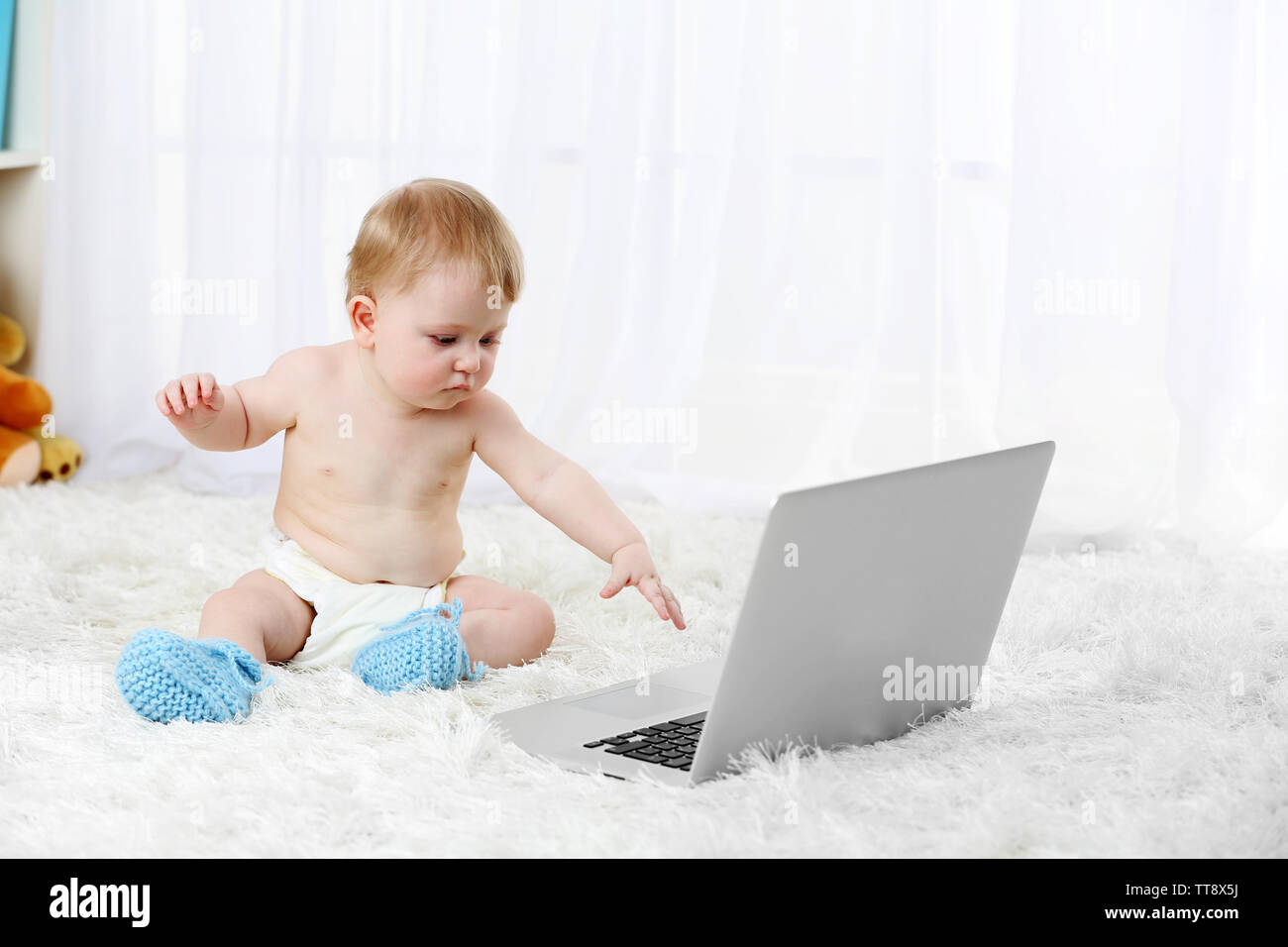 Cute baby boy sitting with laptop on carpet, on light background Stock ...