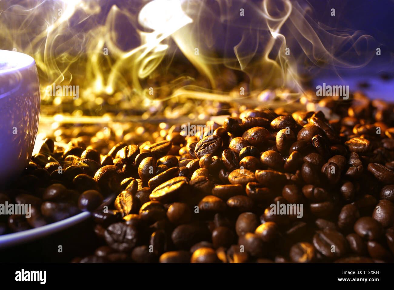 Pile of coffee beans and cup of hot coffee in beam on dark background ...