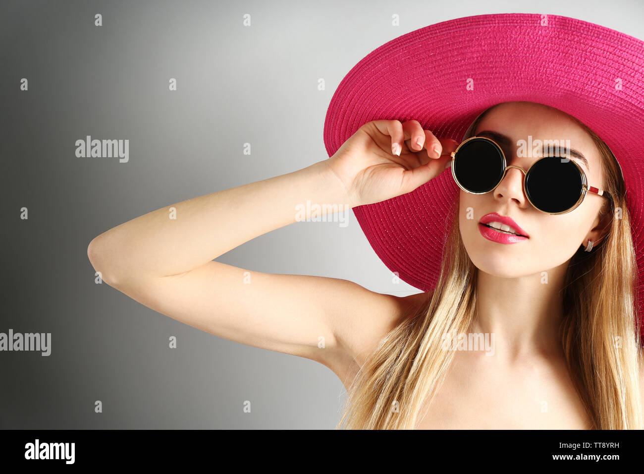 Expressive young model in pink hat with sunglasses on gray background ...