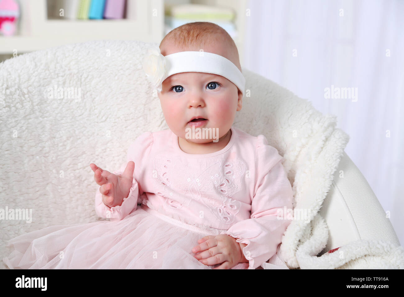 Cute baby girl in pink dress sitting in arm-chair, on home interior ...