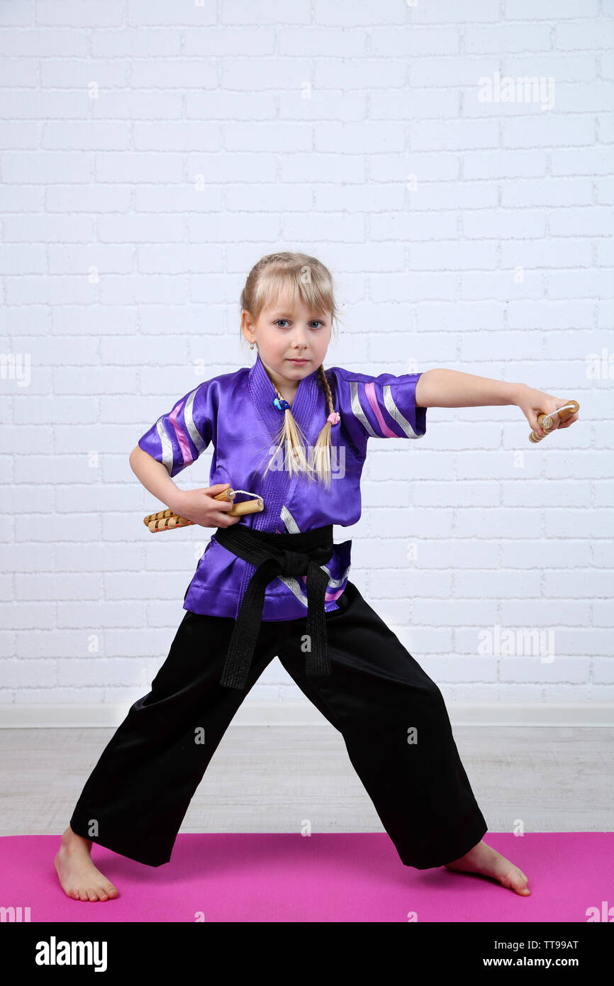 Little girl in kimono doing exercises with nunchaku on wall background ...