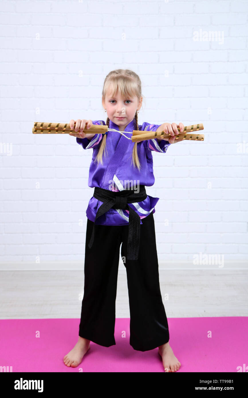 Little girl in kimono doing exercises with nunchaku on wall background ...