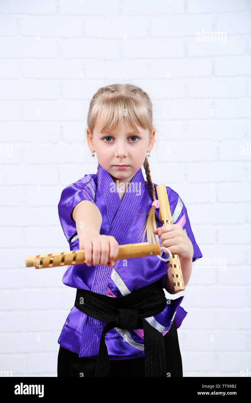 Little girl in kimono doing exercises with nunchaku on wall background ...