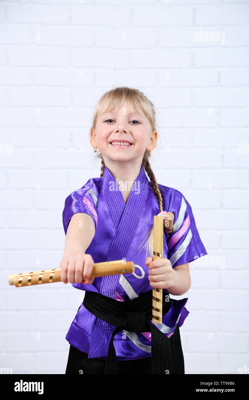 Little girl in kimono doing exercises with nunchaku on wall background ...