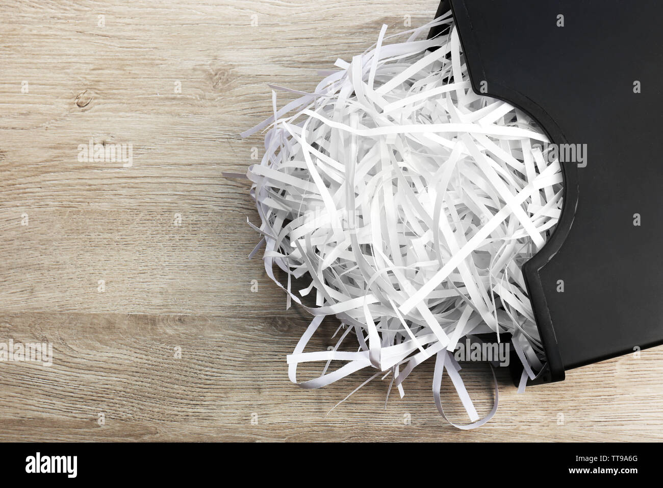 Strips of destroyed paper from shredder in trash can on wooden ...