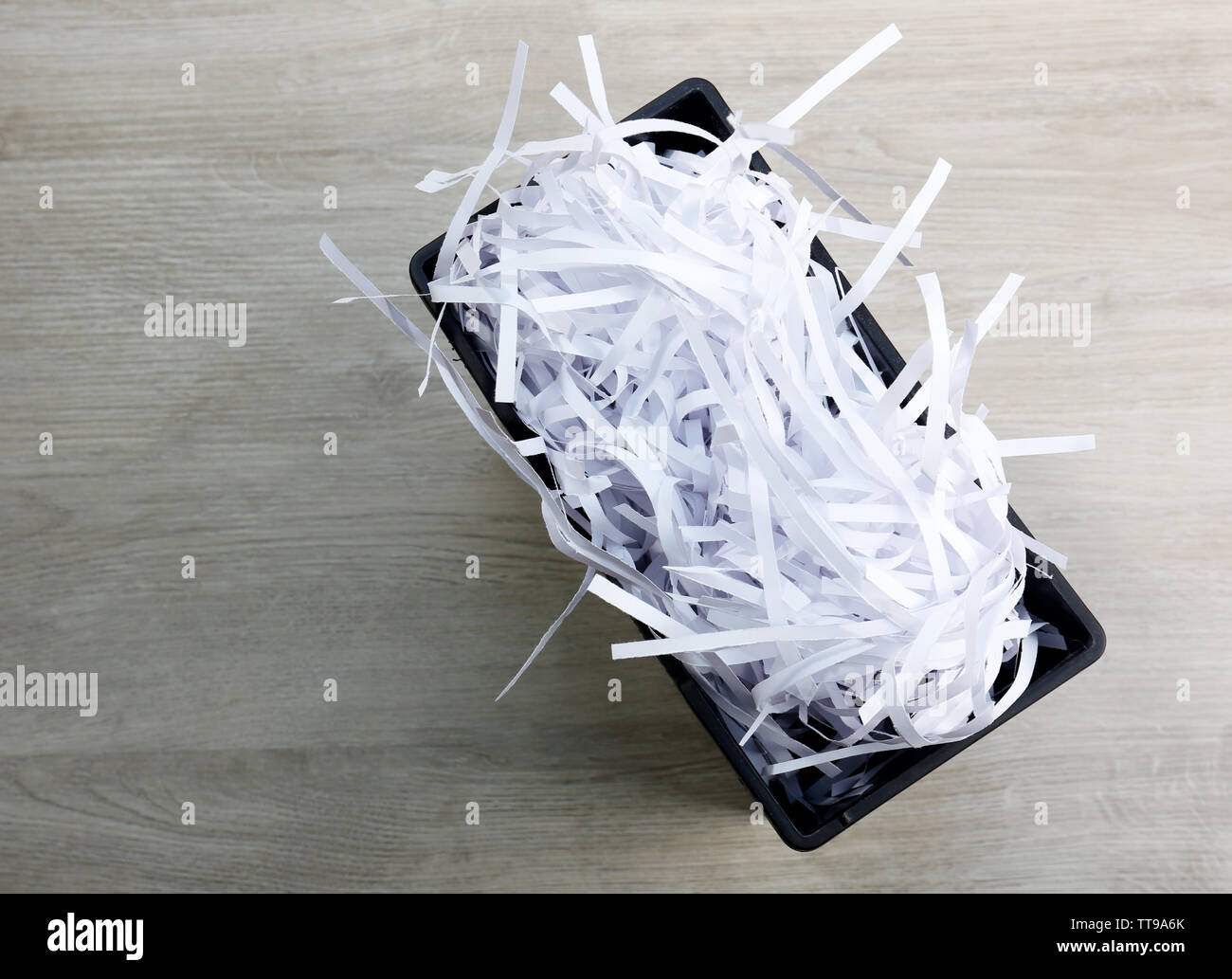 Strips of destroyed paper from shredder in trash can on wooden ...