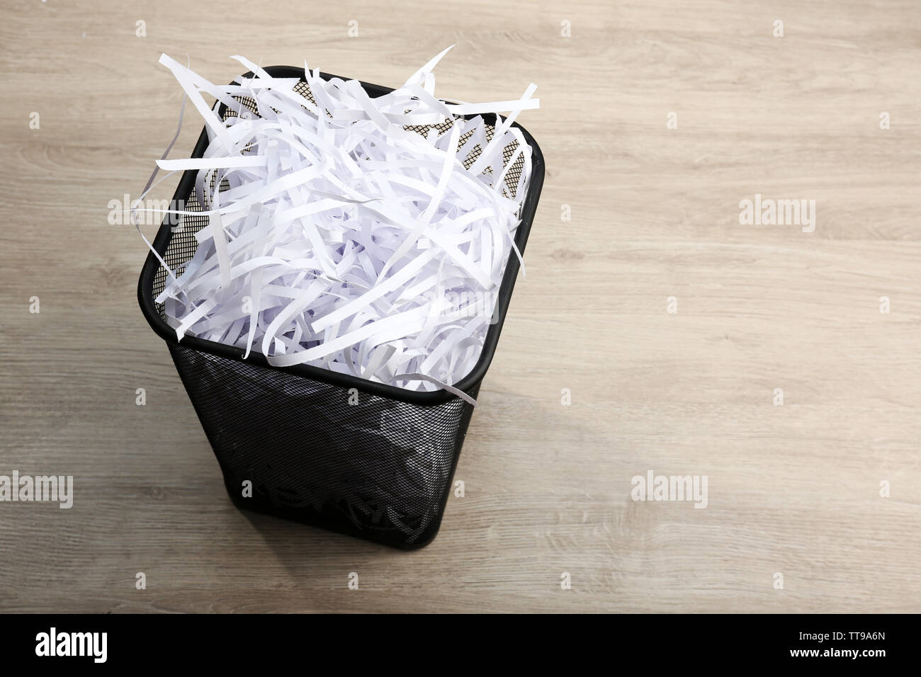 Strips of destroyed paper from shredder in trash can on wooden ...