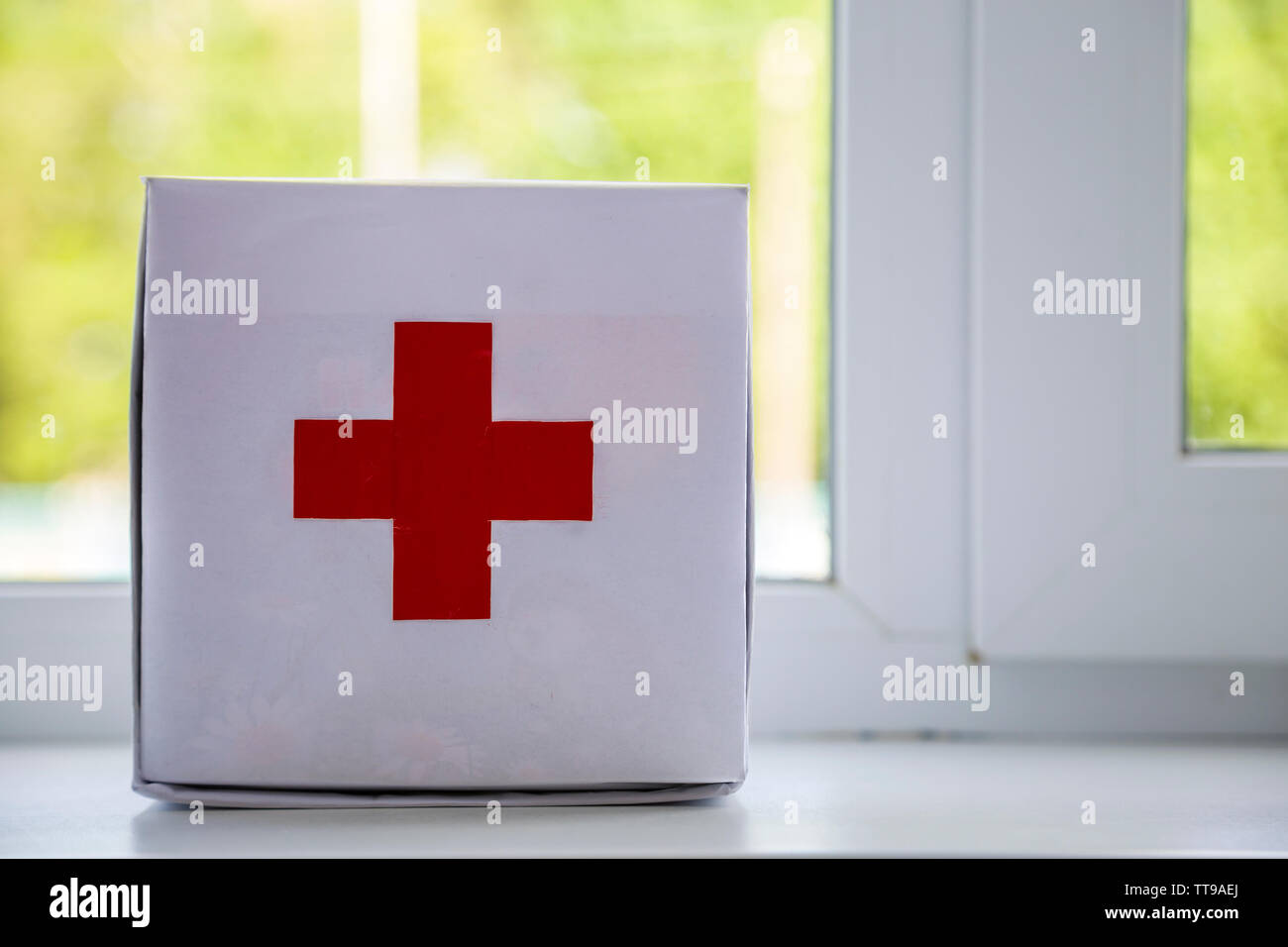 White first aid kit with red cross indoors on windowsill on blurred ...