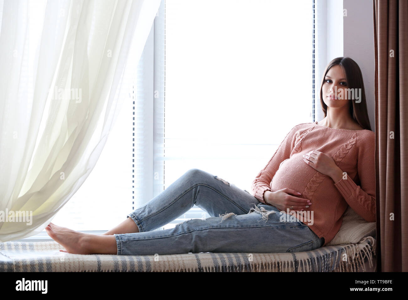 Pregnant woman sitting on windowsill background Stock Photo - Alamy