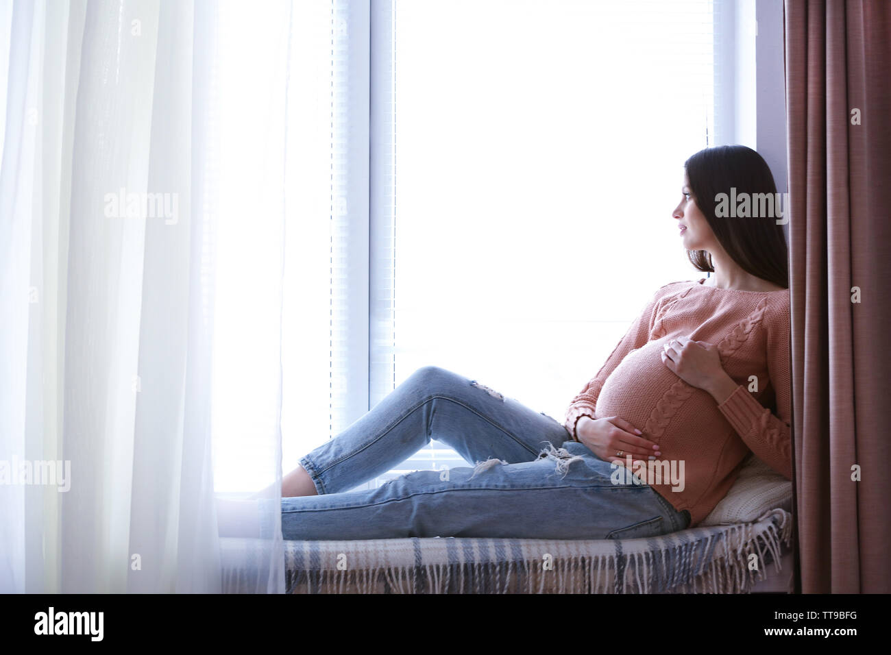 Pregnant woman sitting on windowsill background Stock Photo - Alamy