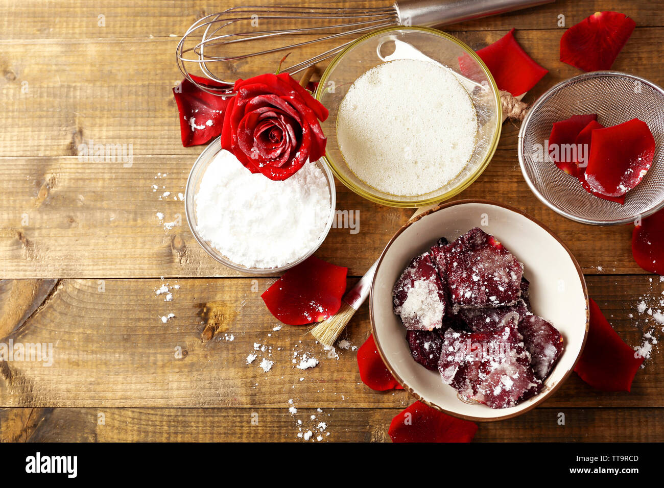 Making candied rose flower petals with egg whites and sugar, on wooden ...